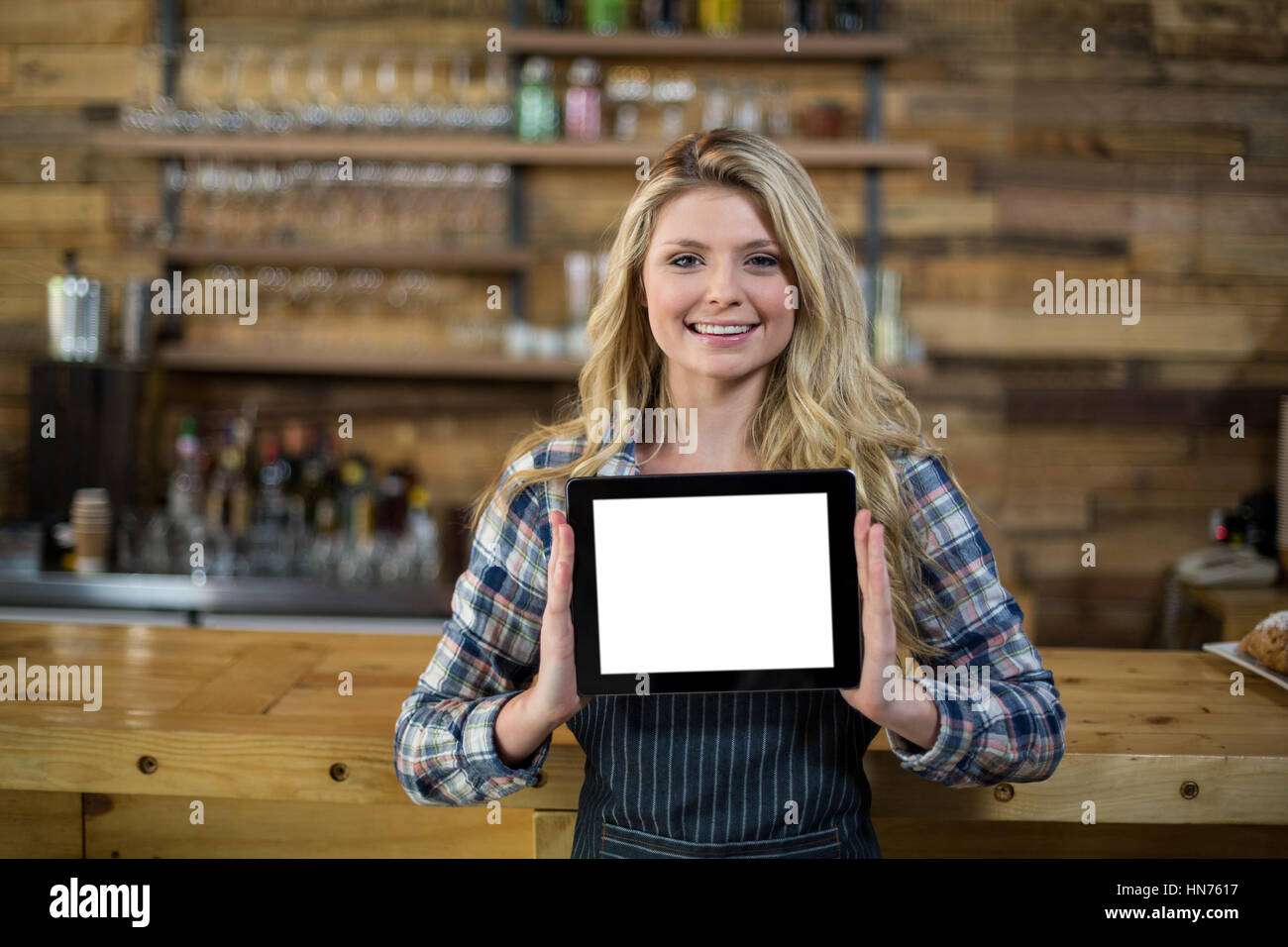 Portrait of smiling waitress standing at counter and showing digital ...