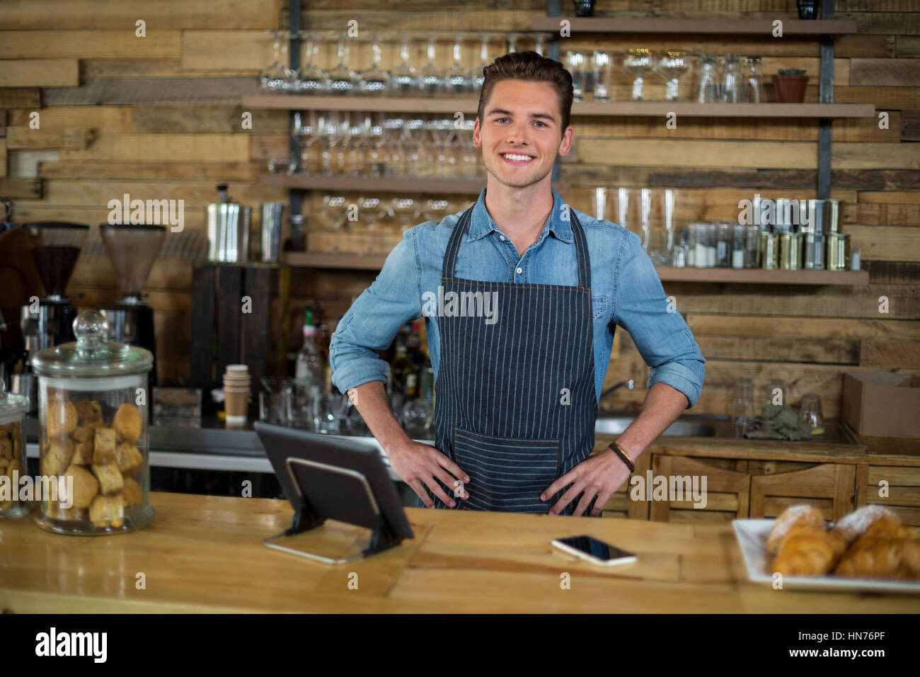 Smiling waiter standing with hands on hip at counter in cafÃƒÂ© Stock ...