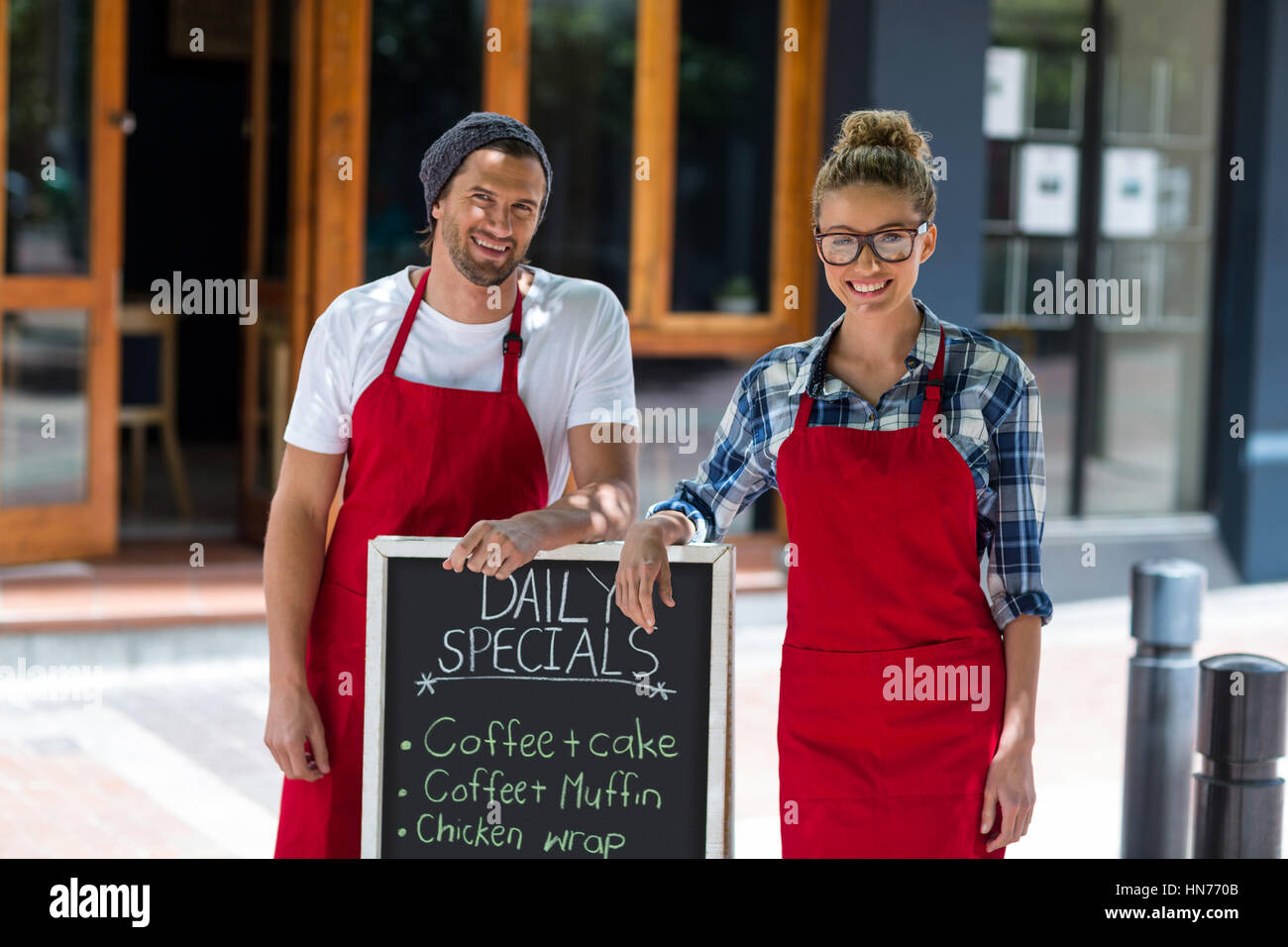 Portrait of smiling waitress and waiter standing with menu sign board ...