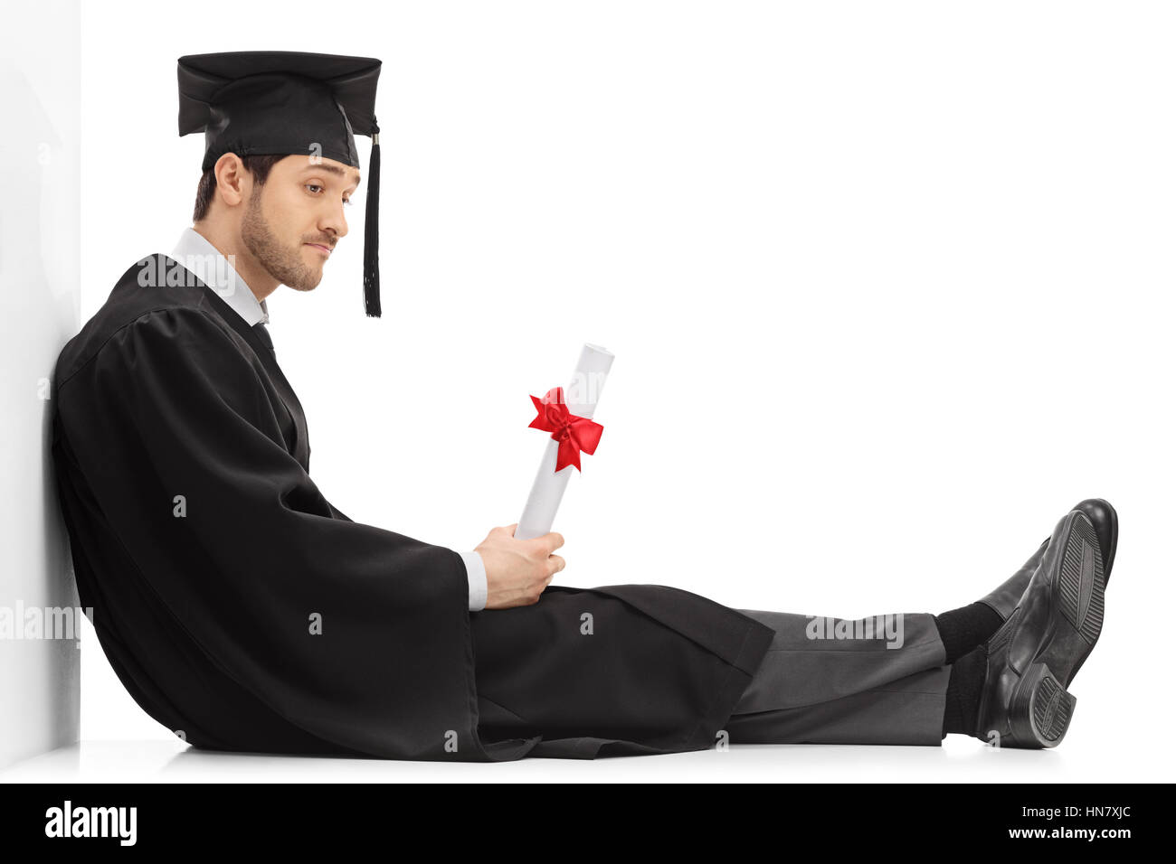 Sad graduate student with a diploma sitting on the floor and leaning on ...