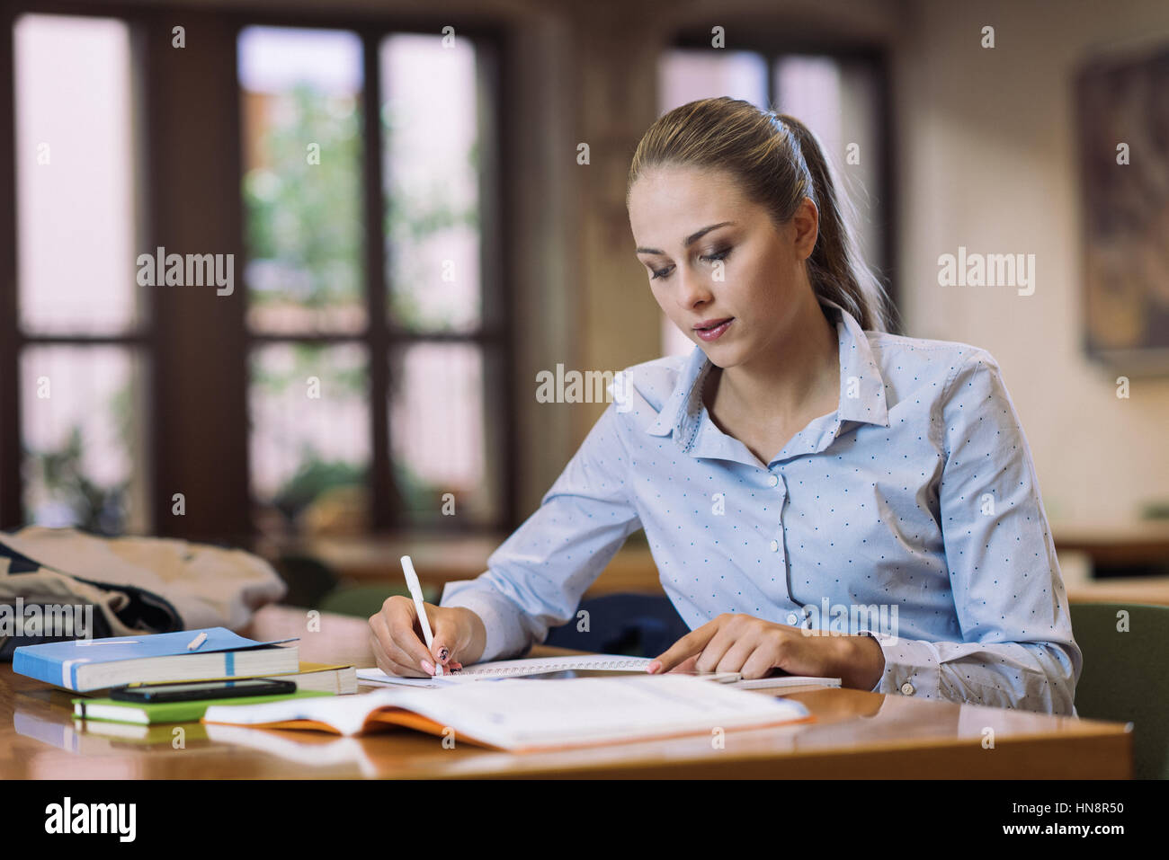 Efficient female student at the library, she is sitting at desk and ...