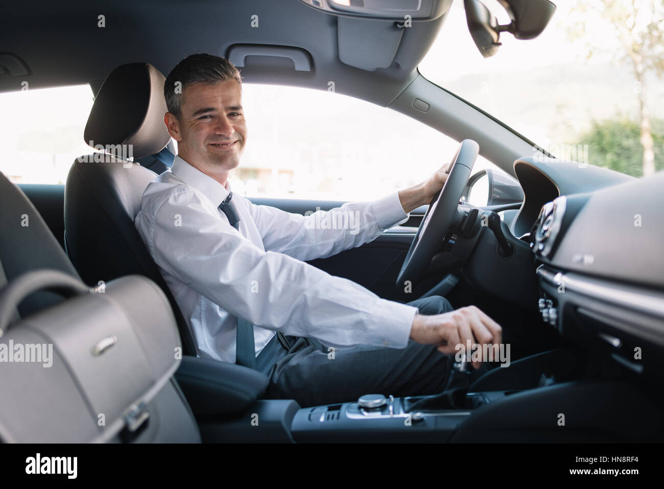 Smiling businessman driving his brand new expensive car, he is shifting ...