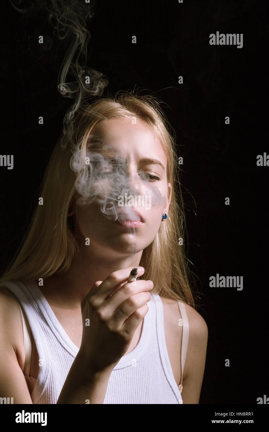 blond young woman smoking joint on black background Stock Photo - Alamy