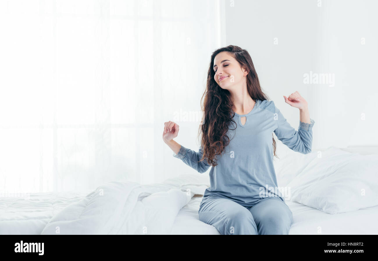 Beautiful woman waking up in her bed in the bedroom, she is stretching ...
