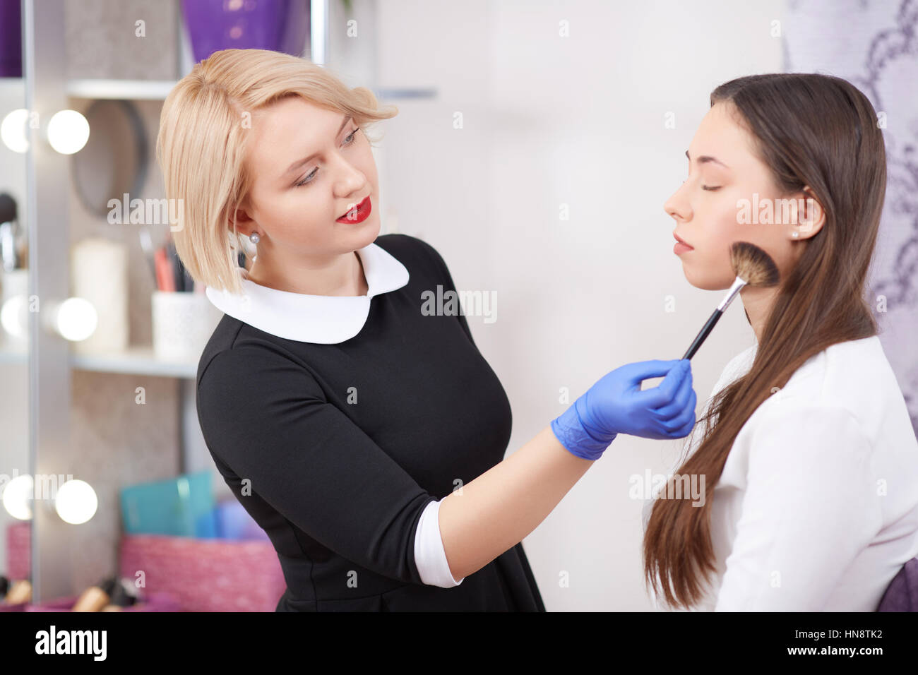 Professional makeup artist wearing black dress and gloves making make ...