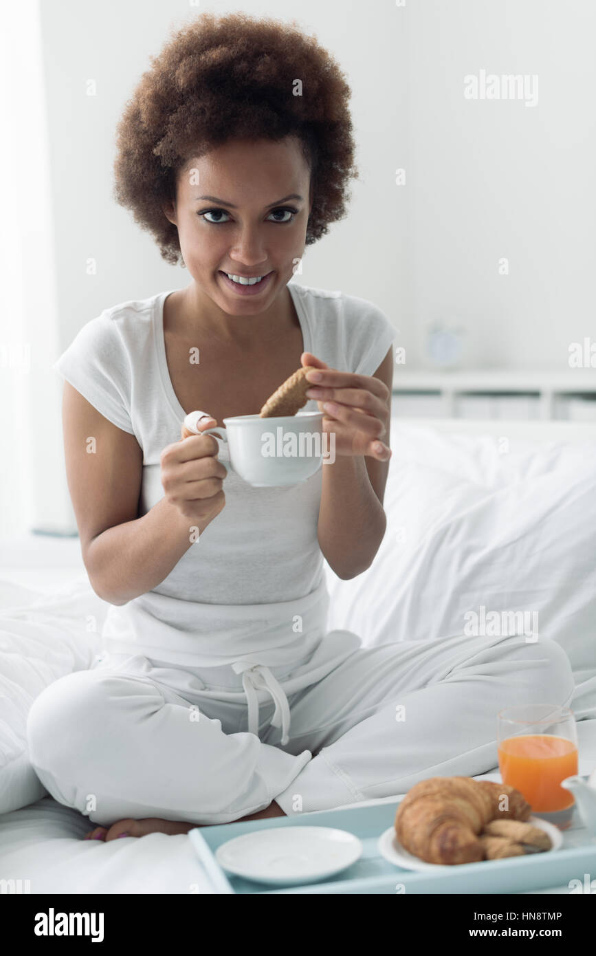 Young african american woman having a relaxing breakfast in bed, she is ...