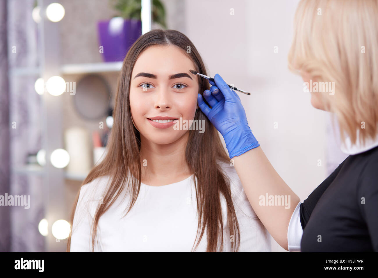 Portrait of professional female stylist in blue gloves making permanent ...