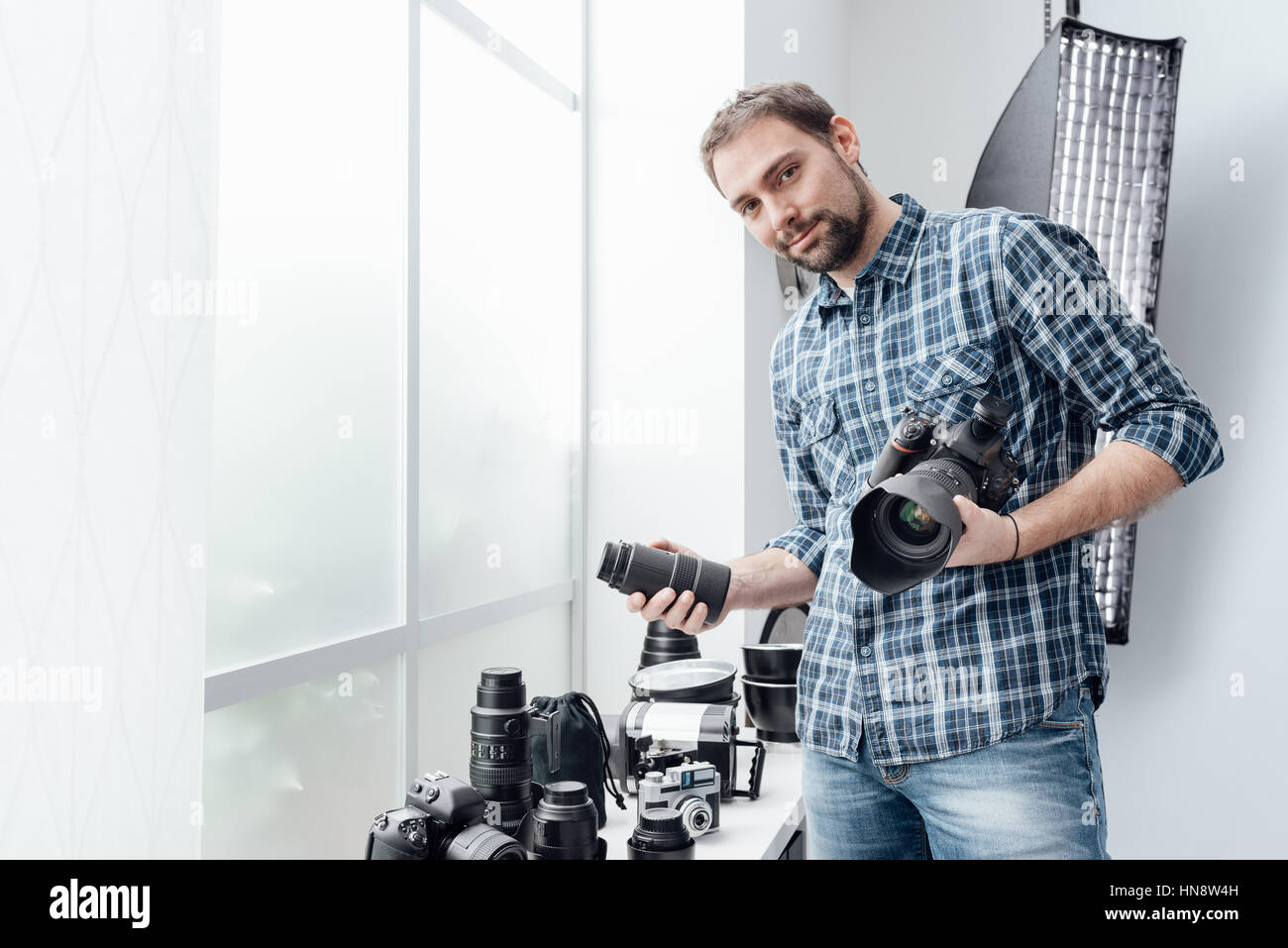 Photographer in his studio, he is holding a digital camera and choosing ...
