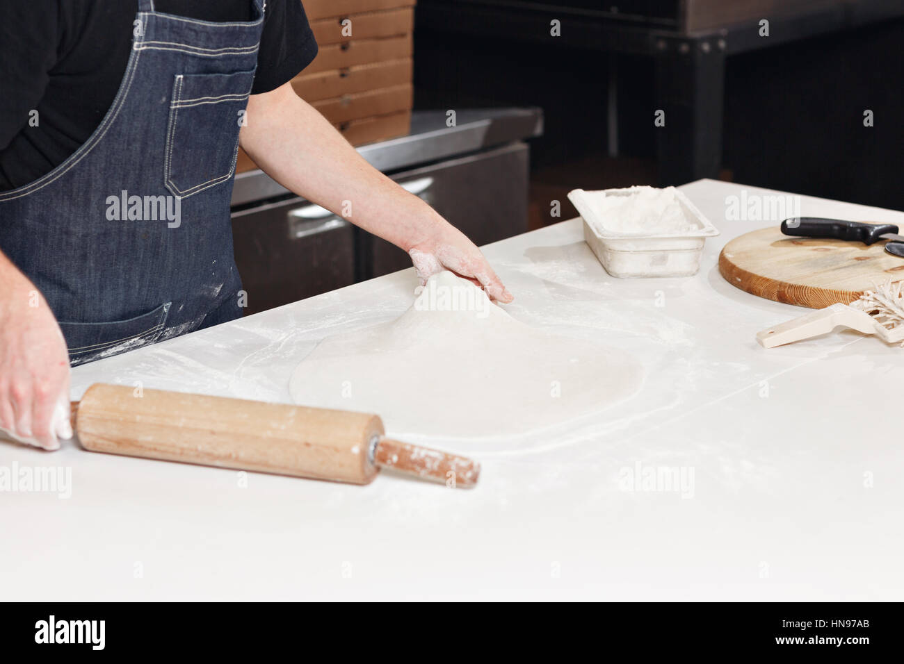 Roll out the dough. Closeup hand of chef baker in uniform blue apron ...