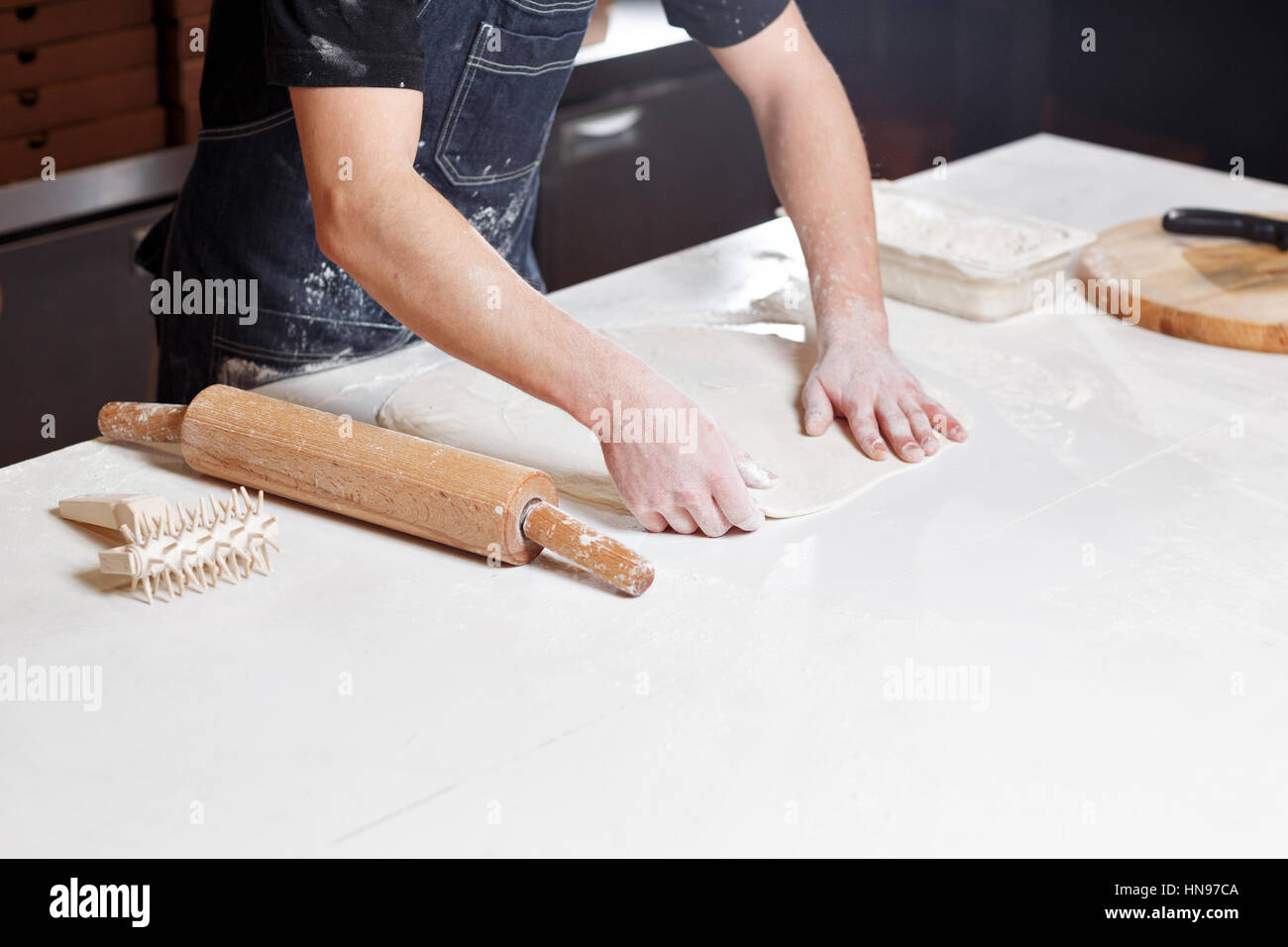 Roll out the dough. Closeup hand of chef baker in uniform blue apron ...