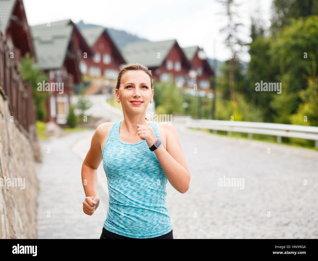 Young smiling fitness woman jogging on cobbled street of hillside town ...
