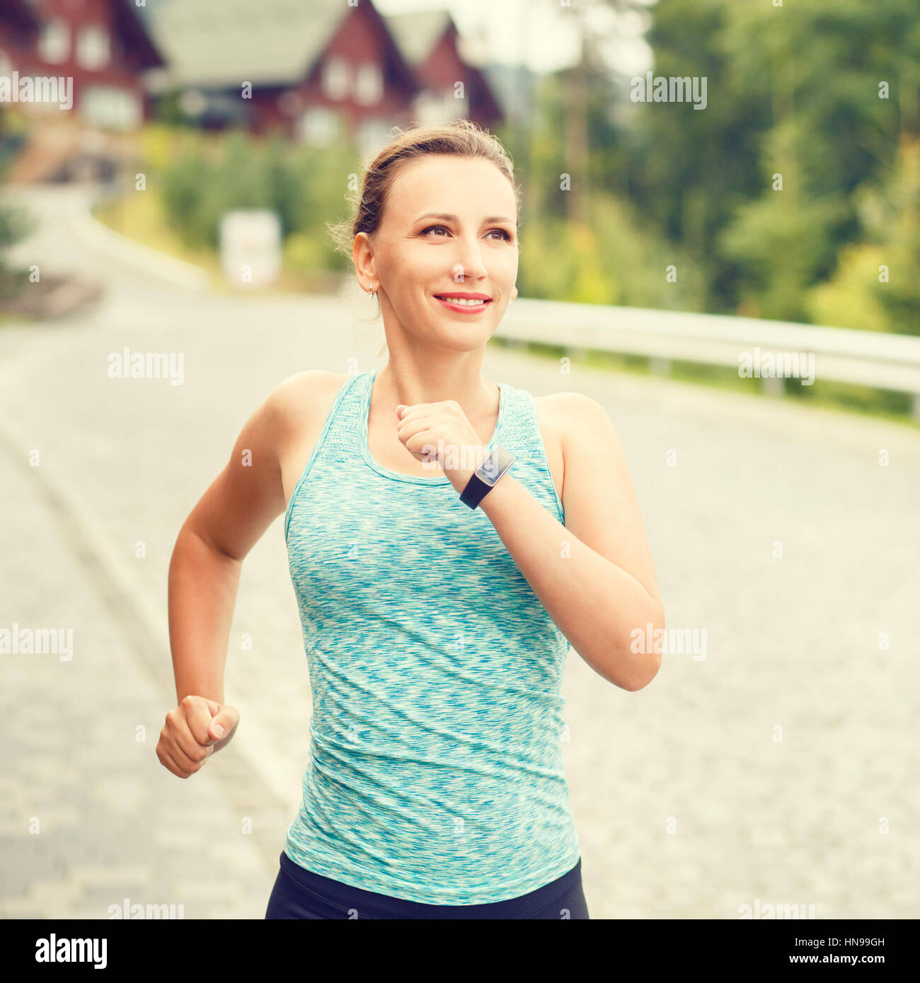 Young smiling fitness woman jogging on cobbled street of hillside town ...