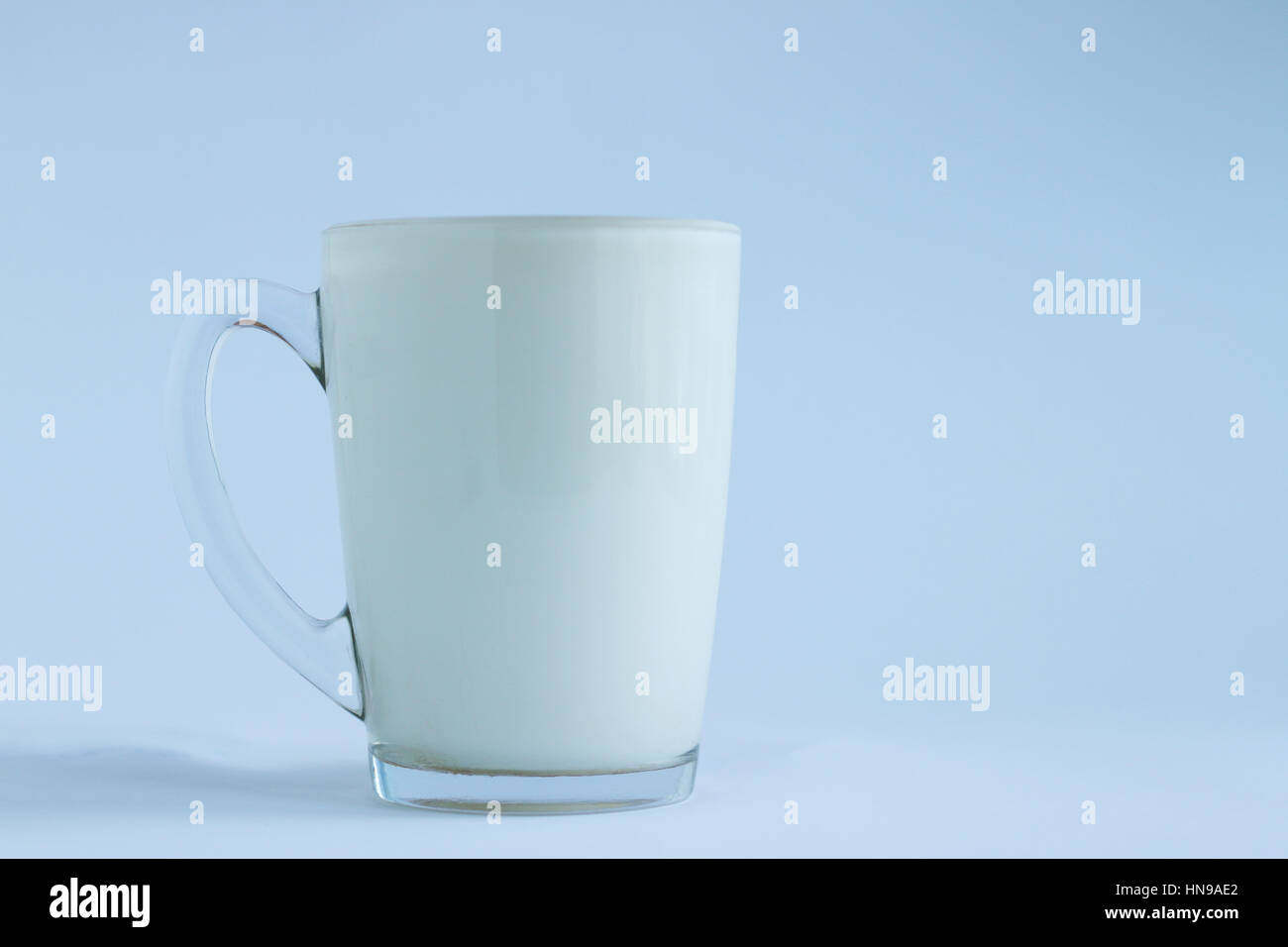 Full transparent glass poured milk on light white and blue background ...