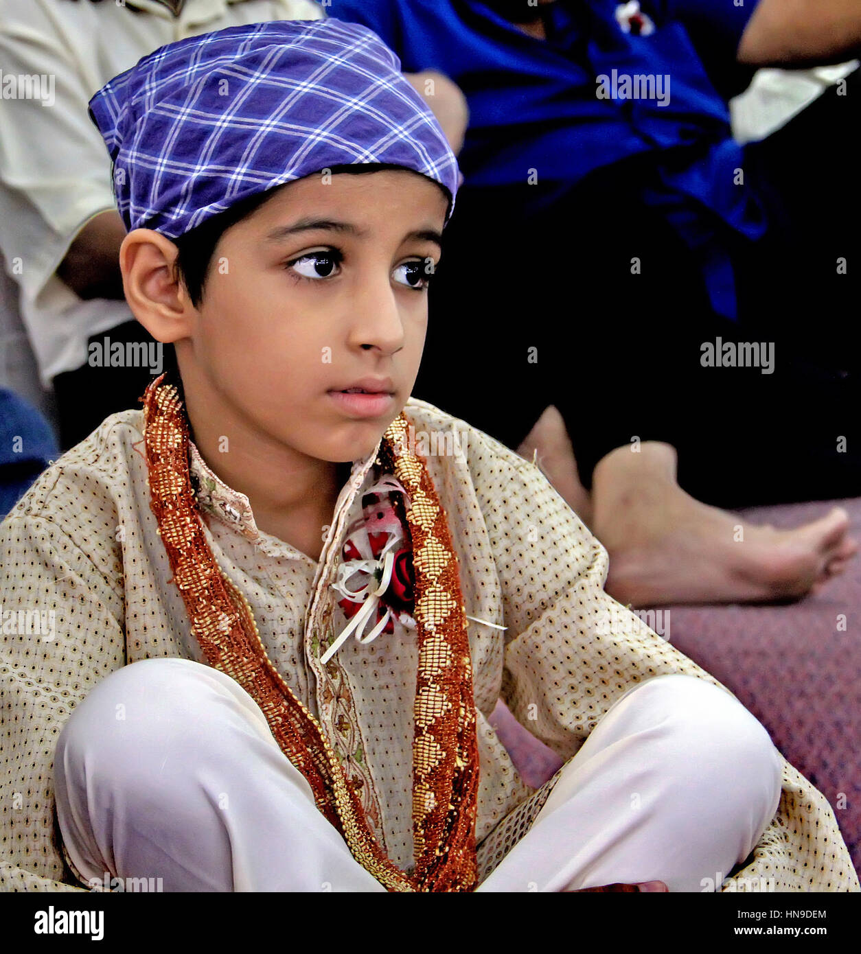 A young Sikh boy sitting wearing blue headwear sitting on the ground at ...