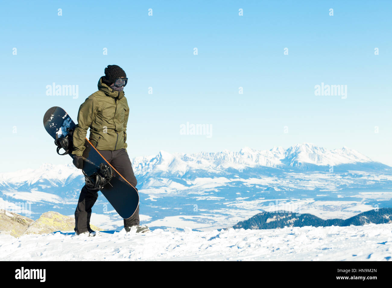 Snowboarder walking at the very top of a mountain with his snowboard in ...