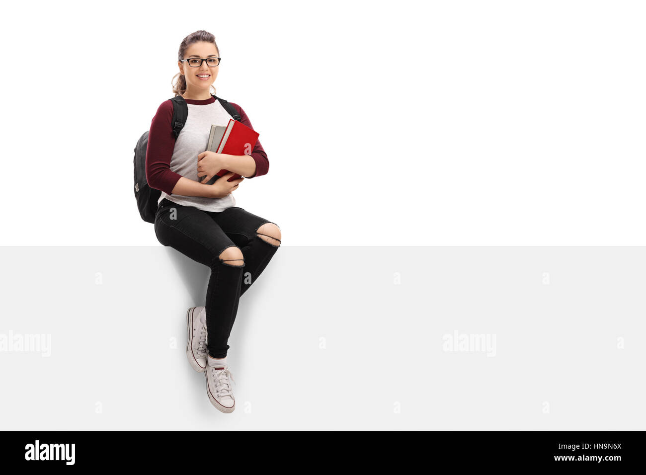 Cheerful female student with a backpack and books sitting on a panel ...