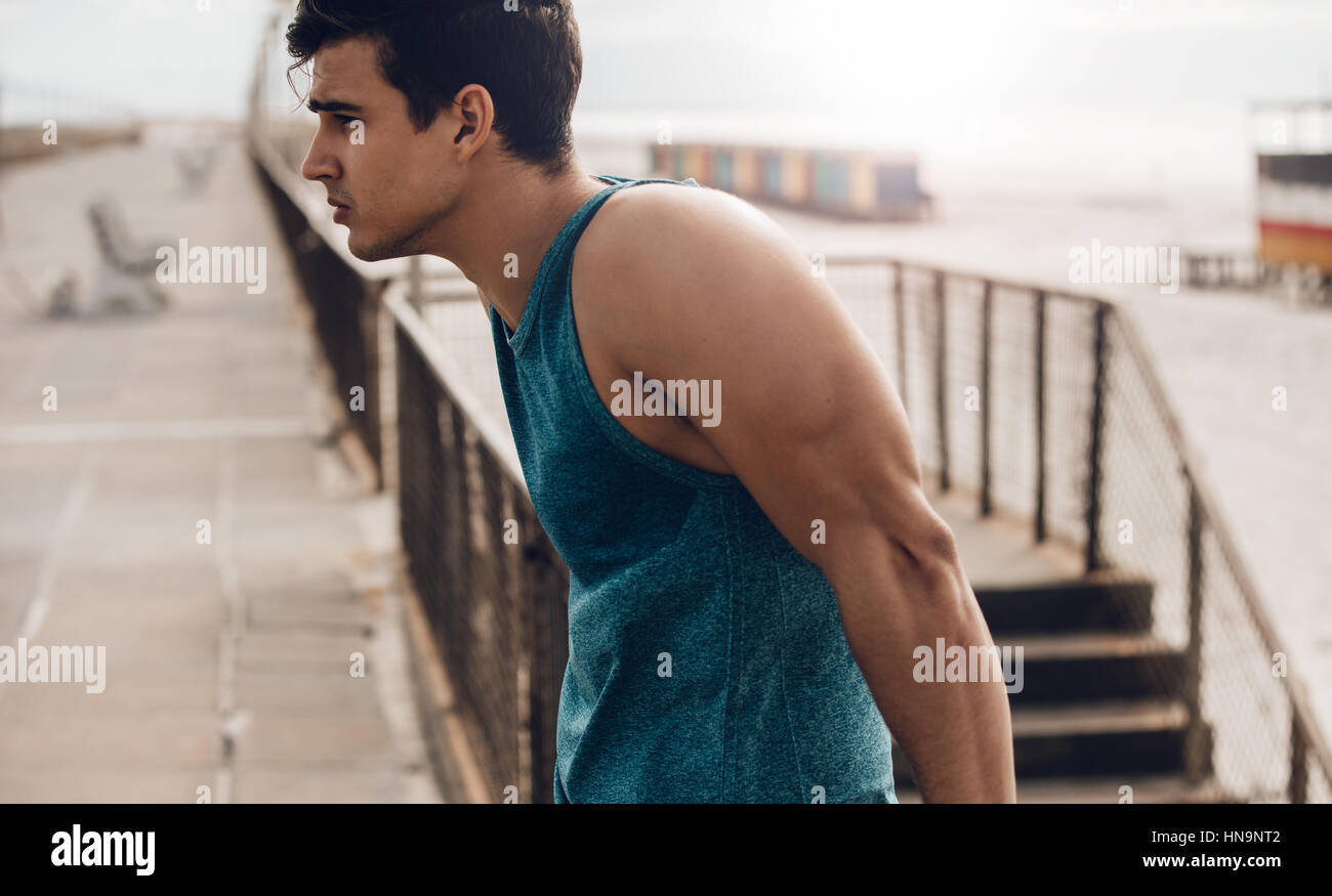 Side view shot of fit young man standing outdoors. Runner taking break ...