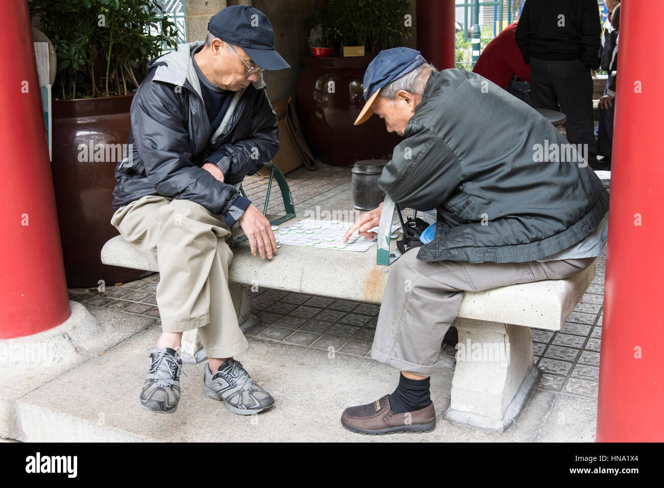 two old men play checkers while on a bench in a park in Hong Kongtwo ...
