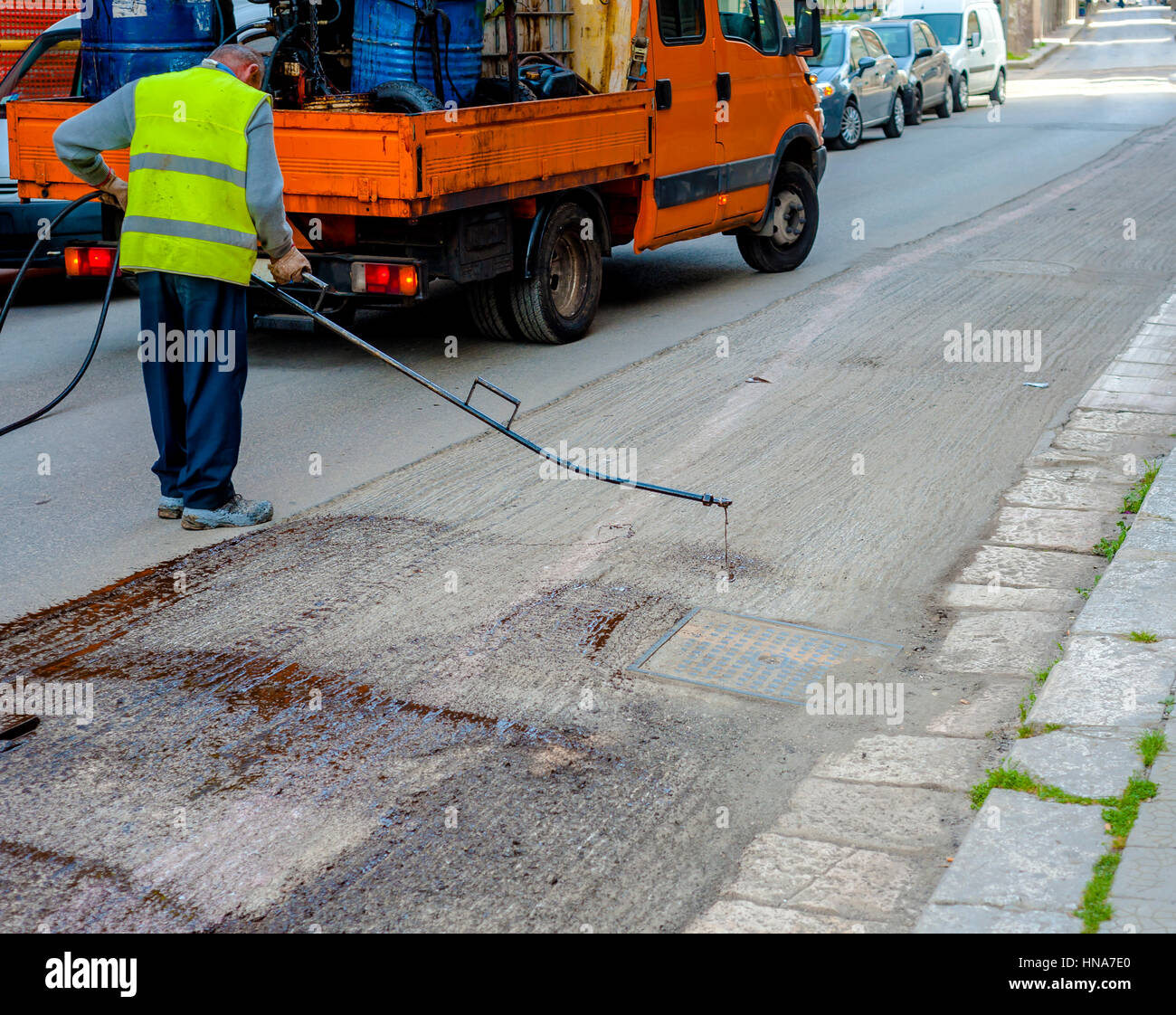 Road worker spraying bitumen emulsion with the hand spray lance before ...