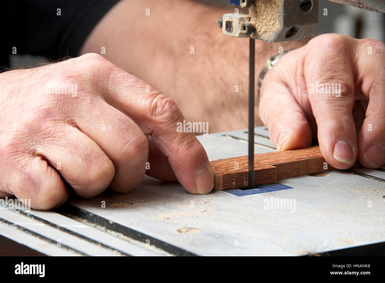 Male hands holding a small piece of wood precision cutting on a table ...
