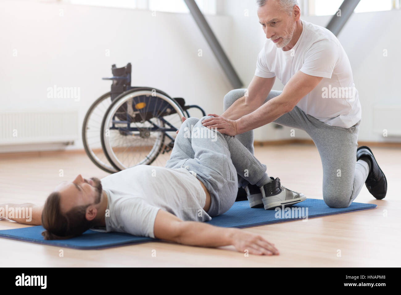 Proficient general practitioner stretching the disabled in the gym ...