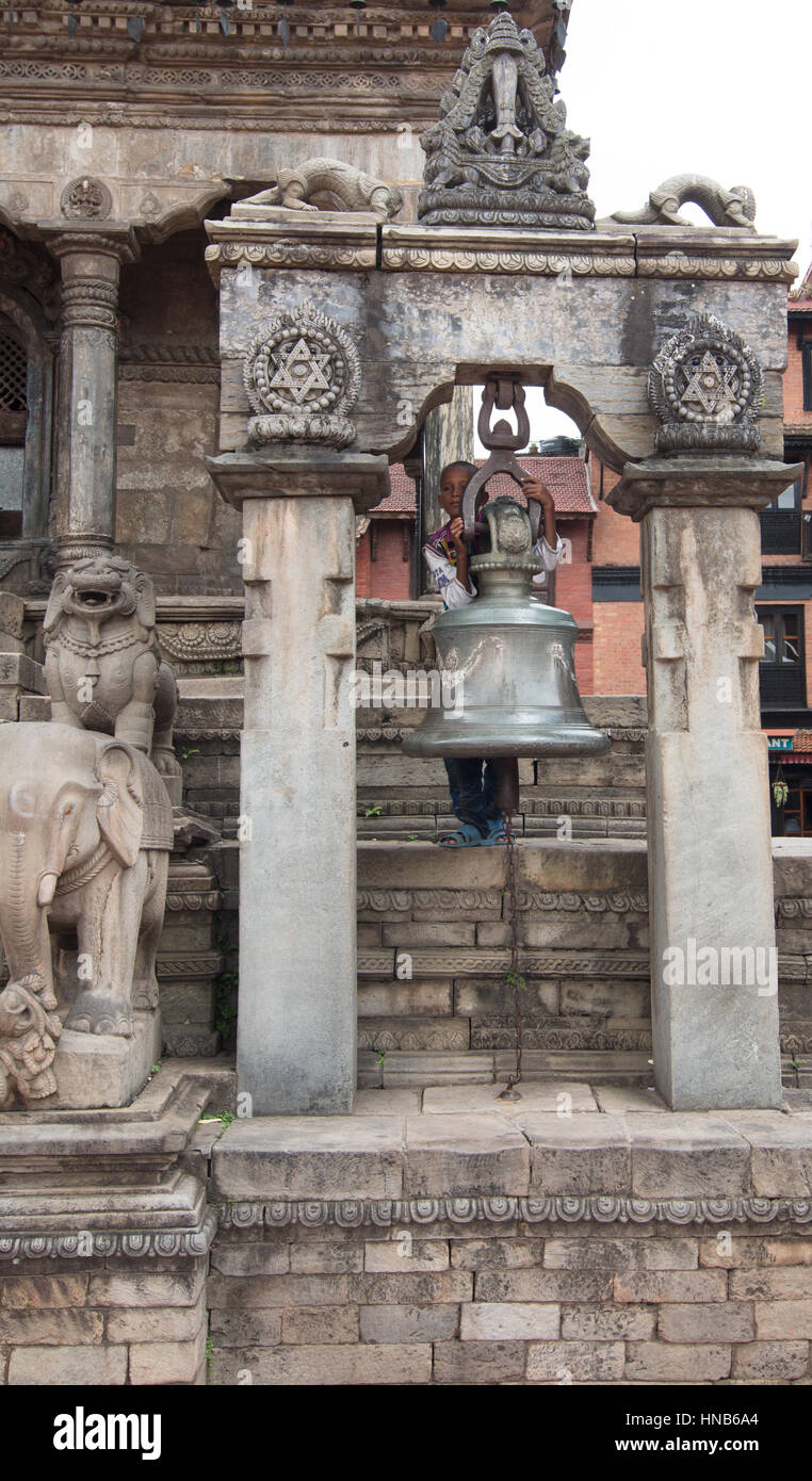Brass bell hanging from ornately carved wooden post outside a temple ...
