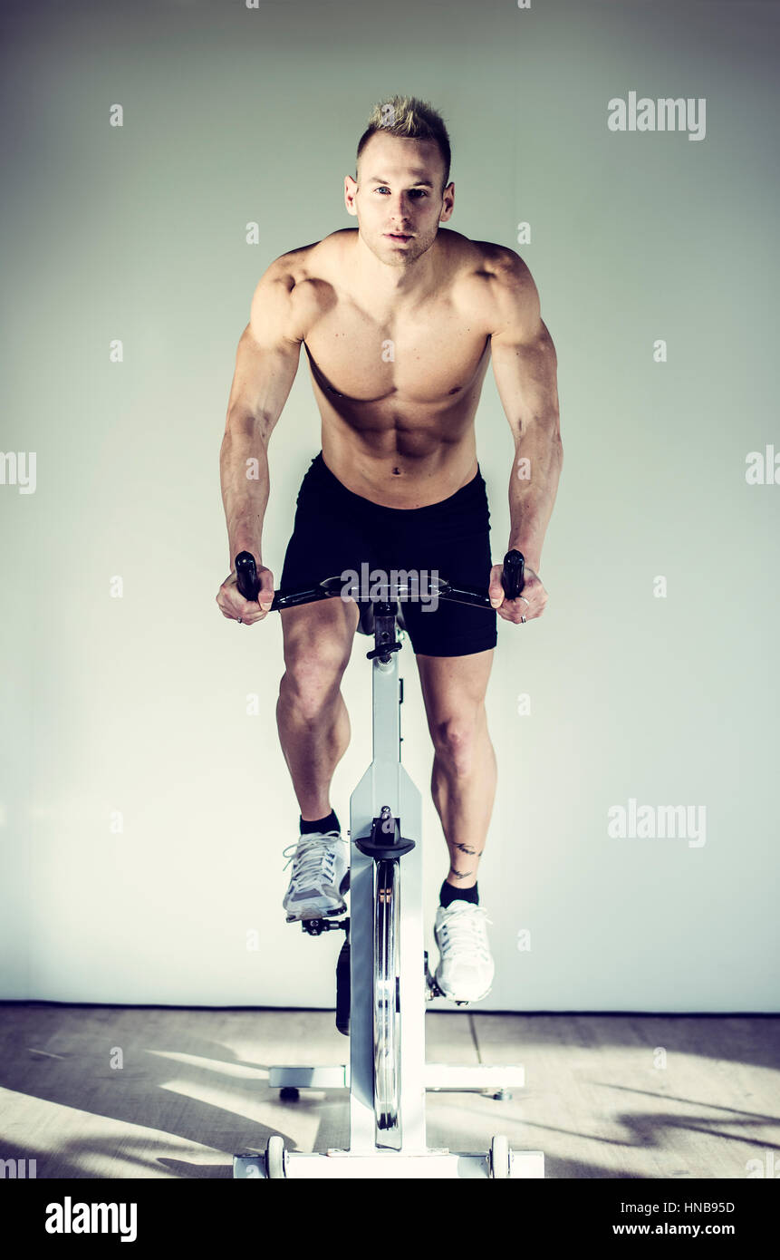 Attractive young man exercising in gym, spinning on stationary bike ...