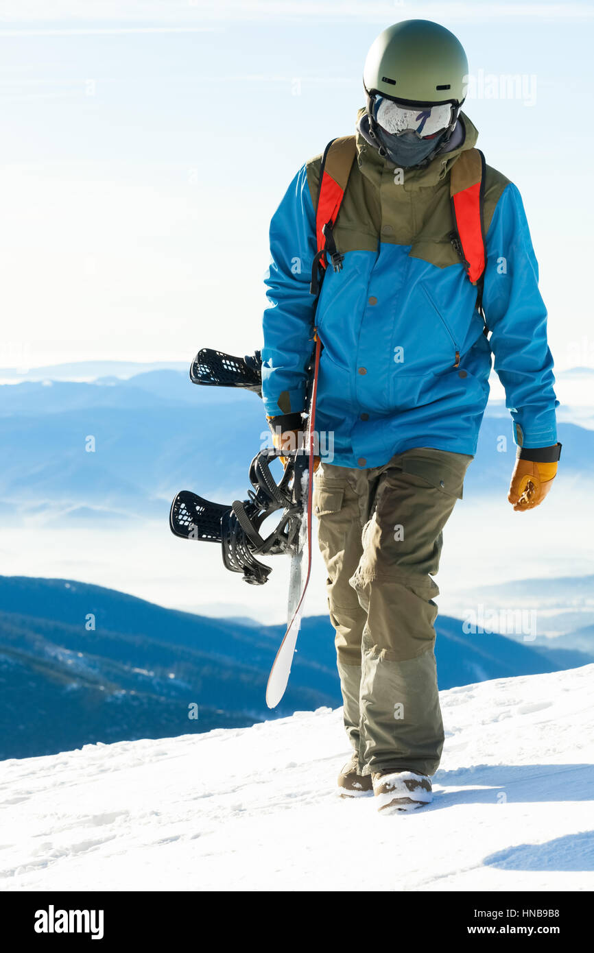 Close up shot of young snowboarder in helmet walking at the very top of ...