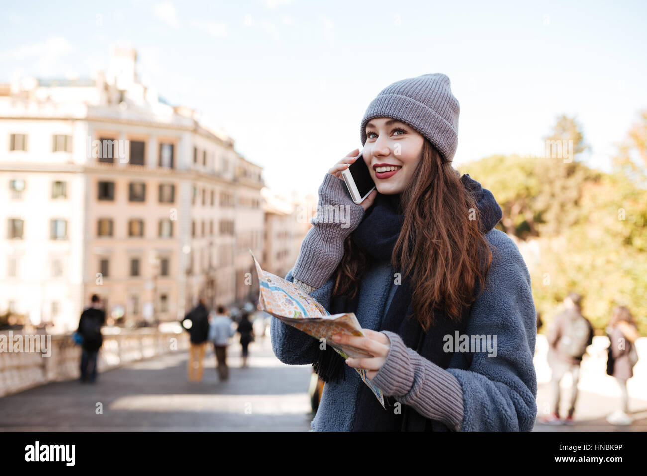 Cheerful beautiful young woman with map talking on mobile phone in the ...
