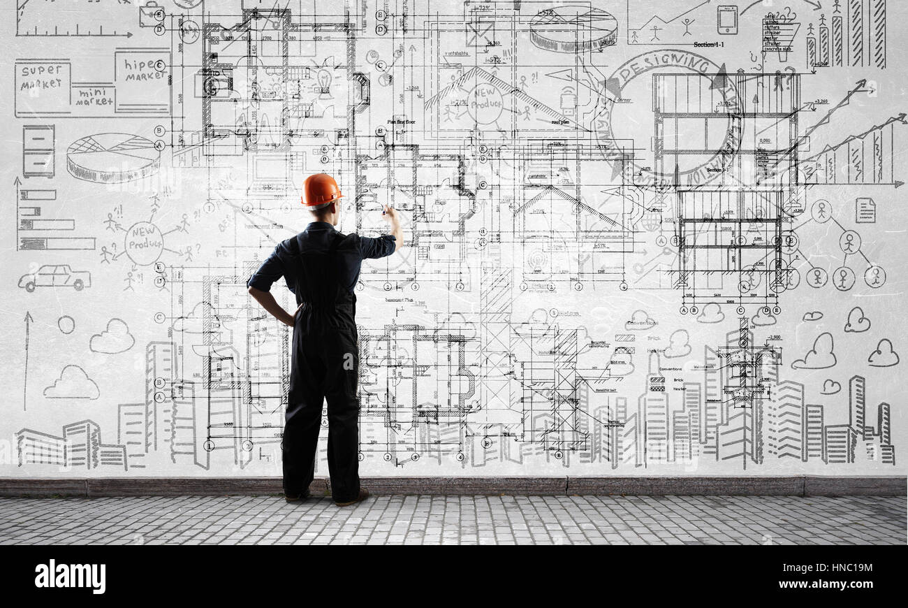 Rear view of engineer man in helmet and overall sketching construction ...