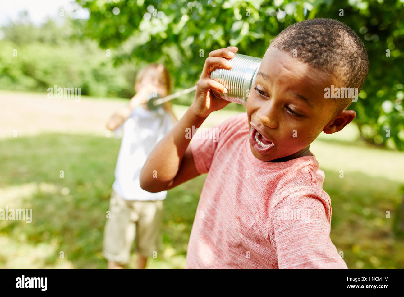 African boy calling friend with tin can telephone in summer in the park ...