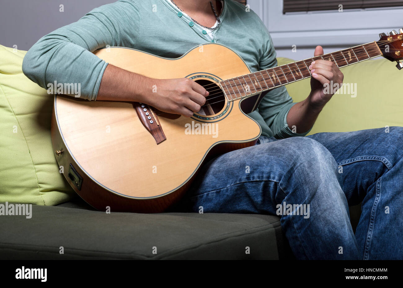 Guy seated on couch playing electric acoustic guitar, unplugged session ...