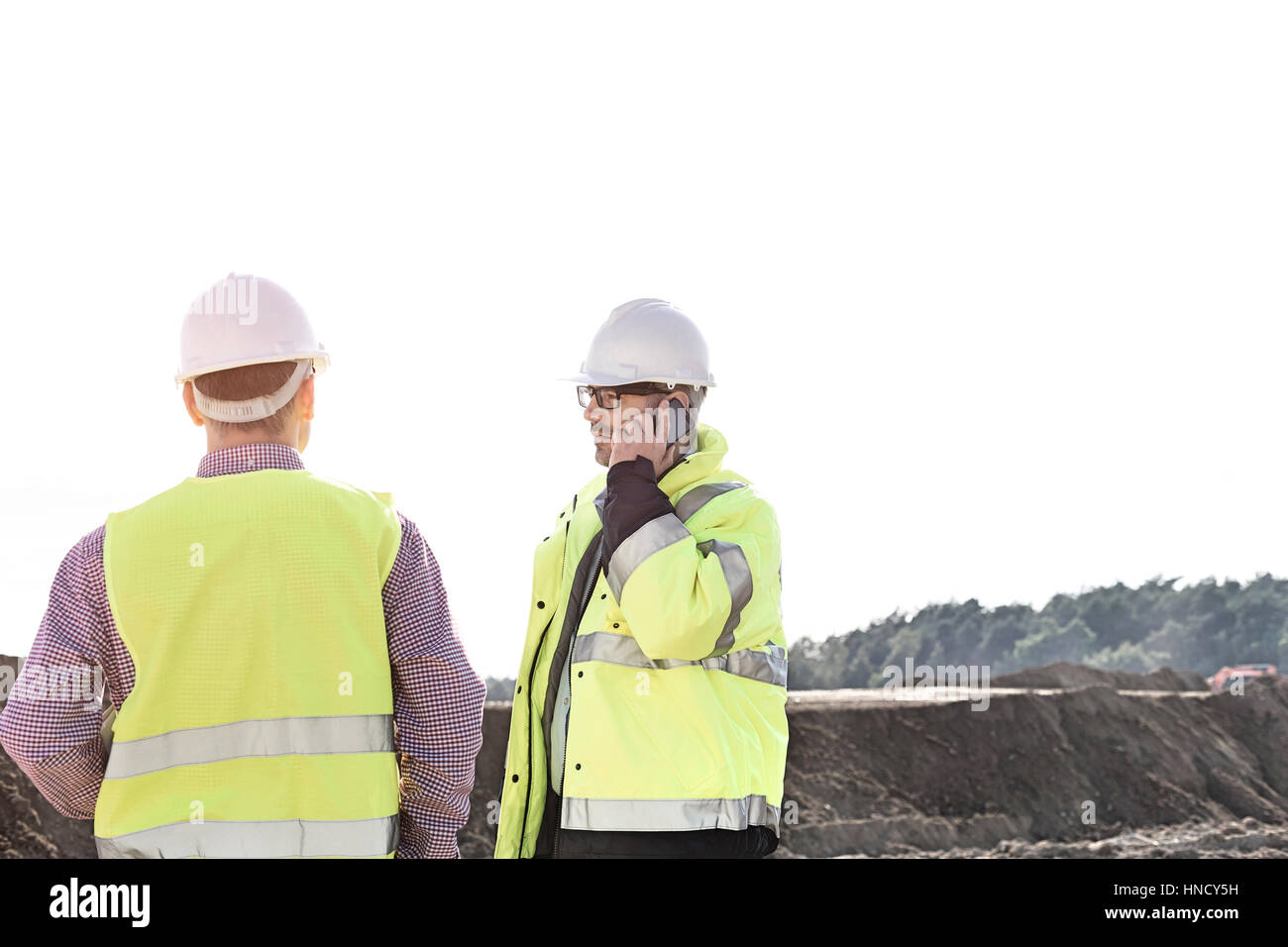 Male engineer using mobile phone while standing with colleague at ...