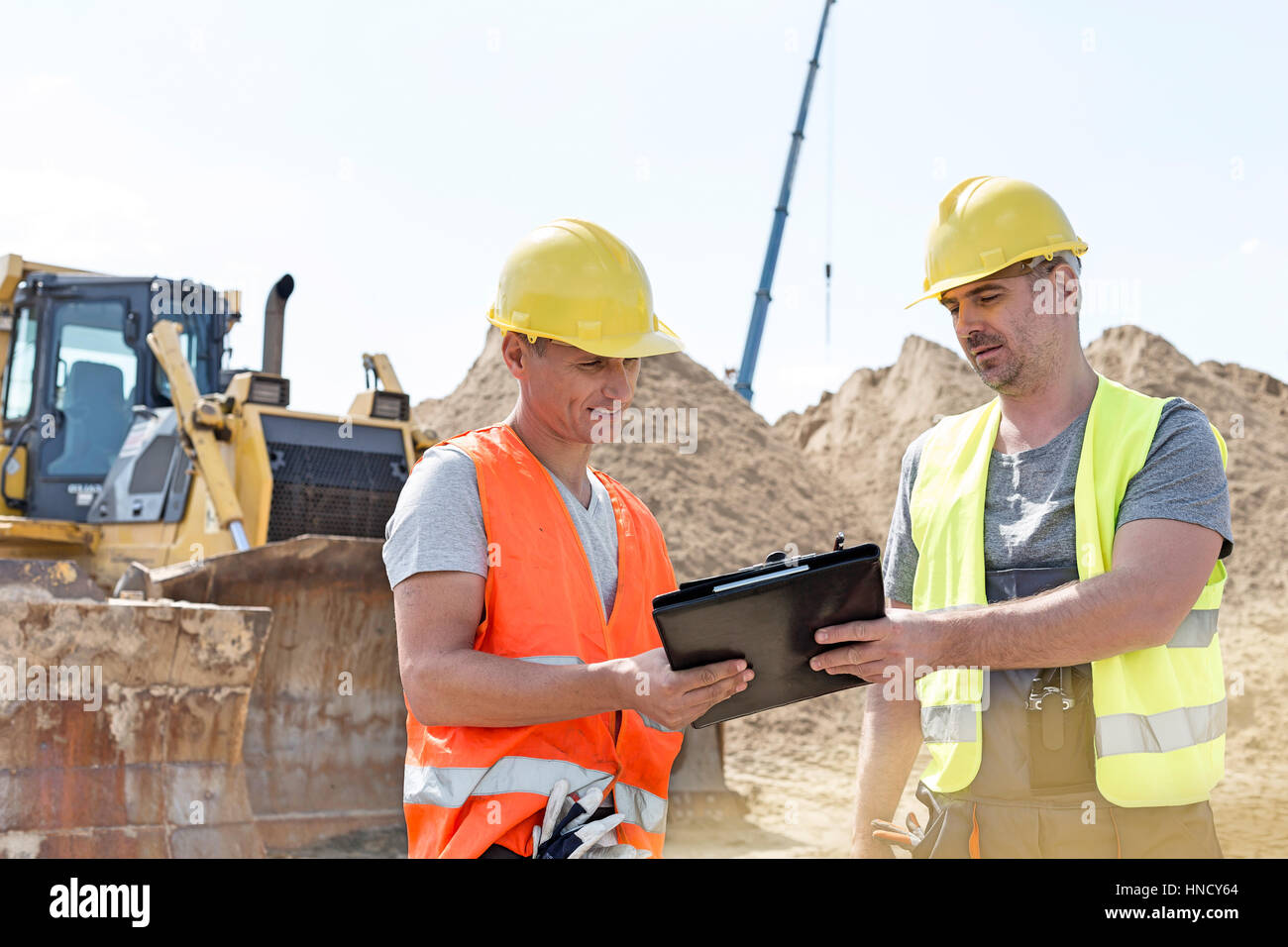 Engineers reading clipboard at construction site against clear sky ...