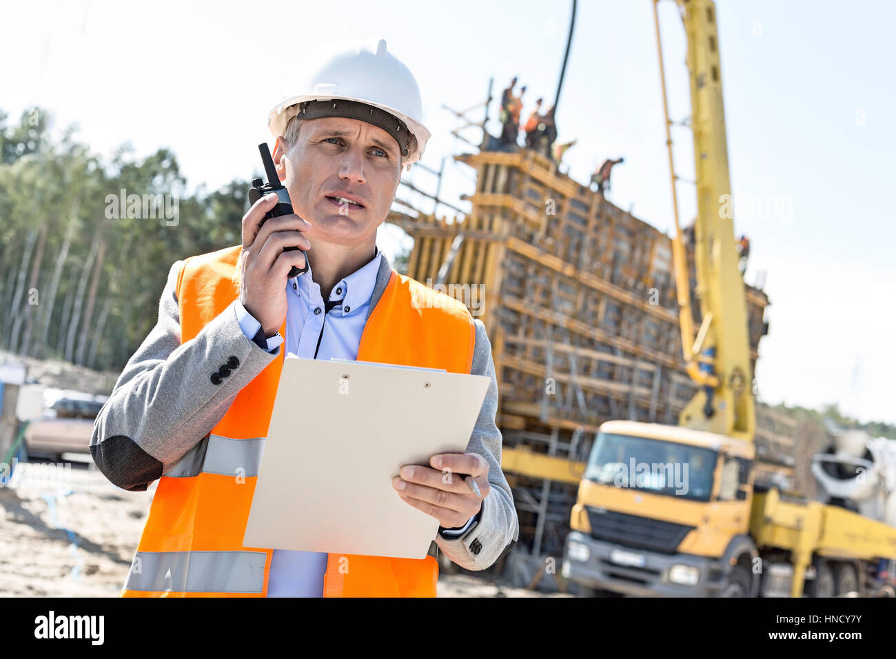 Supervisor using walkie-talkie while holding clipboard at construction ...