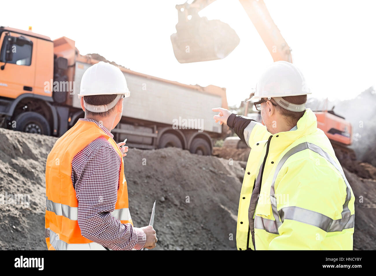 Engineer pointing at vehicles while discussing at construction site ...