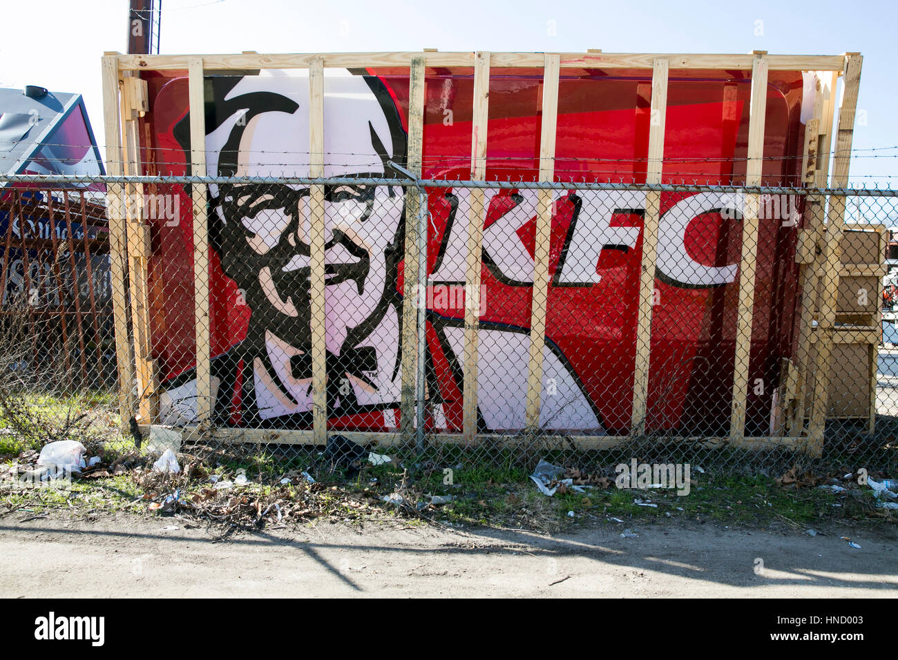 A Kentucky Fried Chicken (KFC) restaurant sign leaning against a fence ...