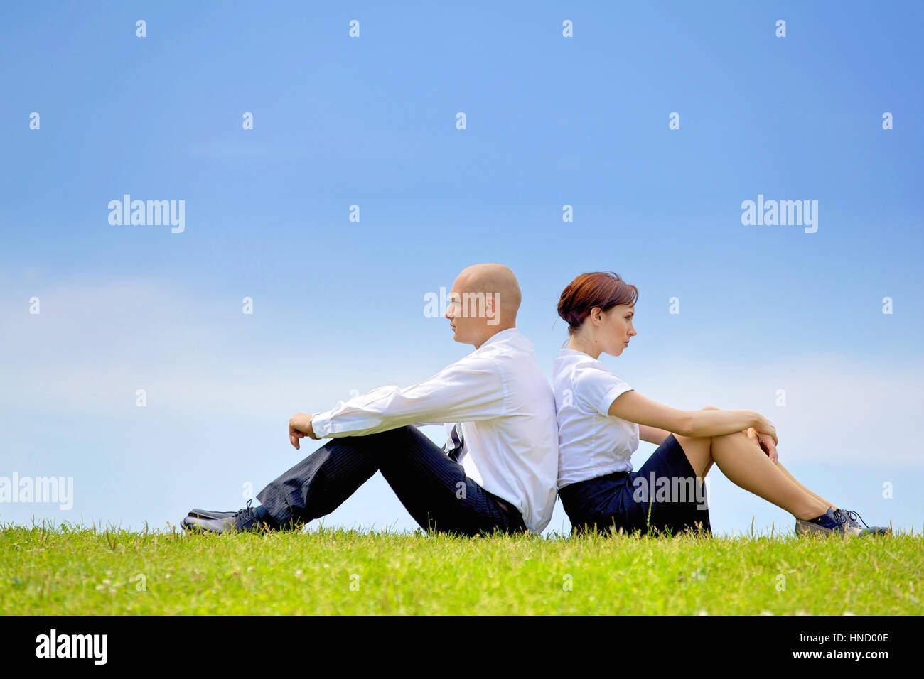 Business couple sitting back to back on grass Stock Photo - Alamy