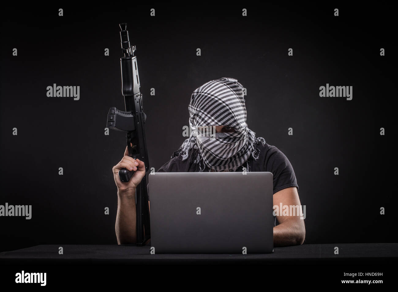 Hacker with gun over laptop on black background Stock Photo - Alamy