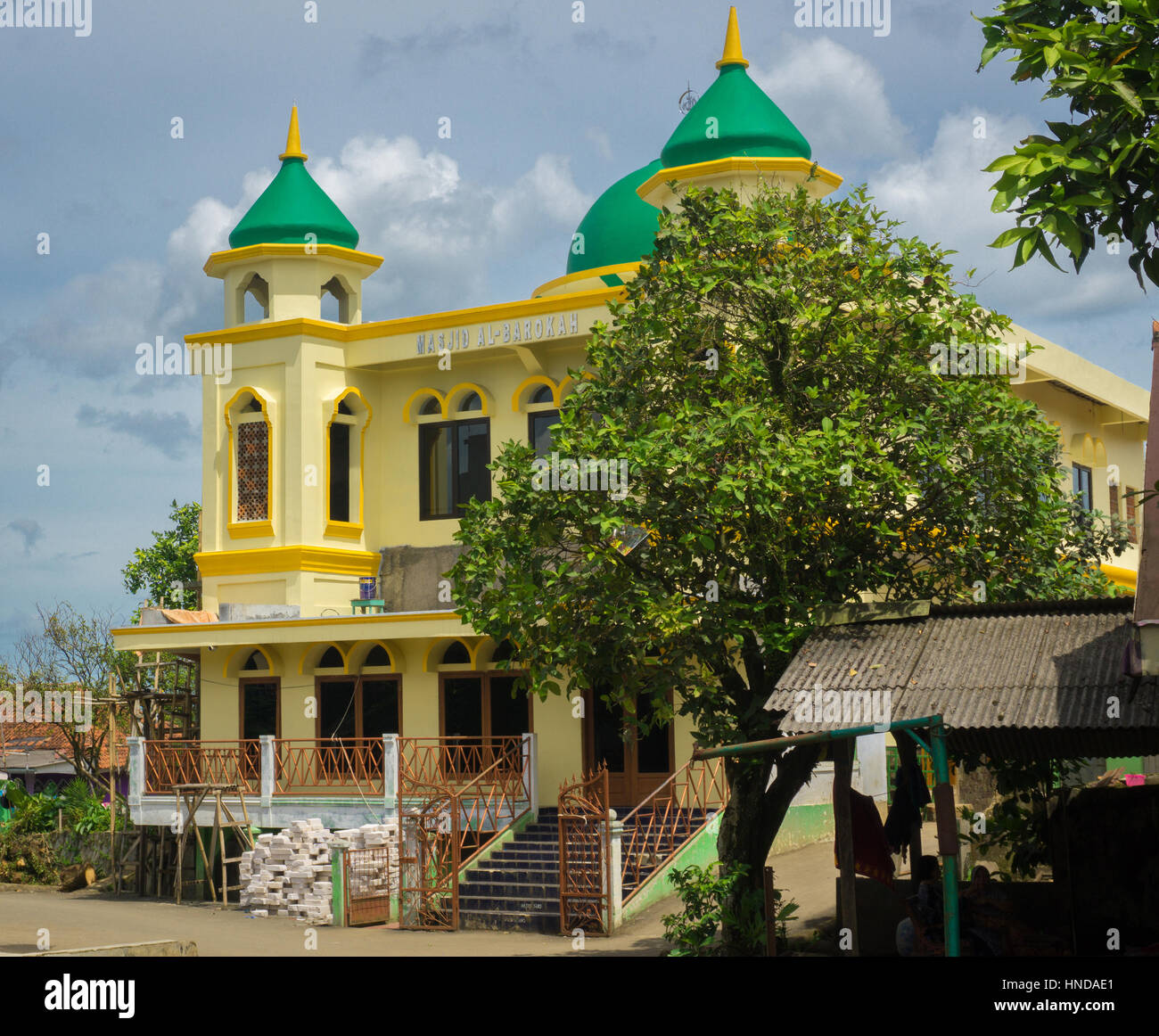 A big yellow mosque with green dome near a big tree photo taken in ...