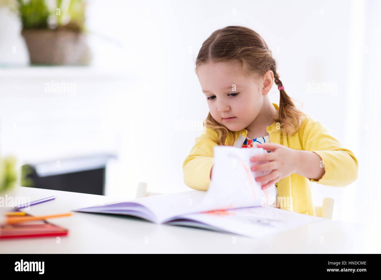 Cute little girl doing homework, reading a book, coloring pages ...