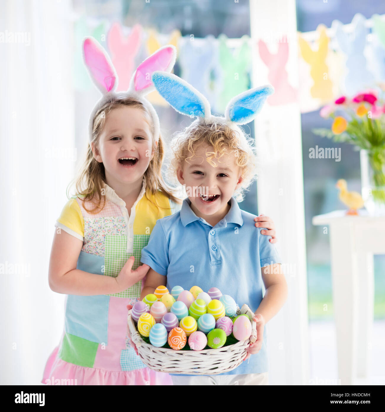 Little boy and girl in bunny ears holding a basket with colorful Easter ...
