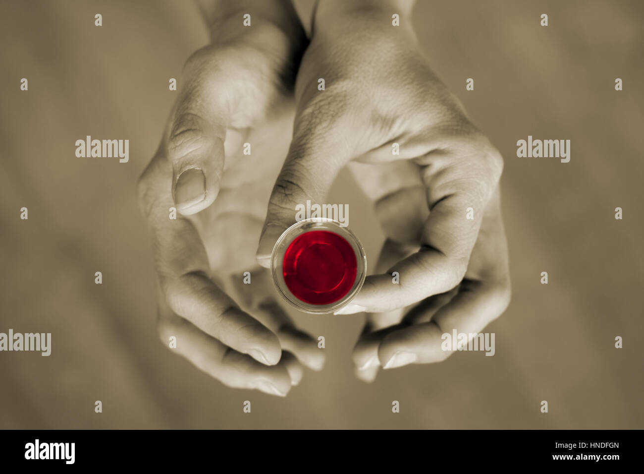 Toned image of hands holding a communion cup filled with wine or juice ...