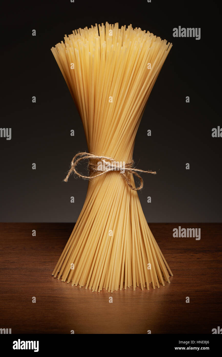 Dry spaghetti pasta tied up with rope on dark wooden table on grey ...