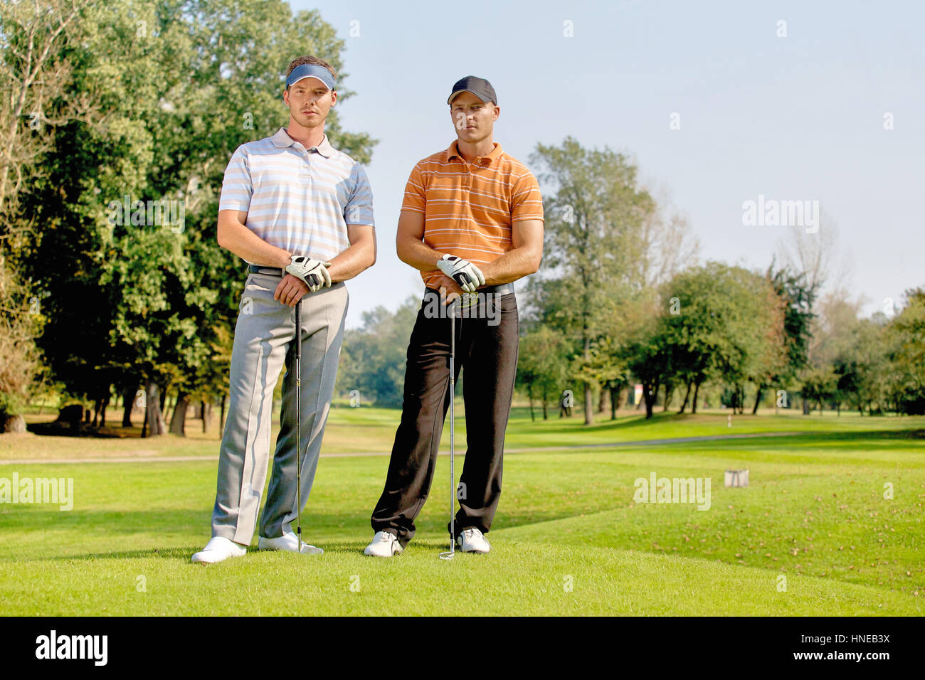 Portrait of young men standing with golf sticks on golf course Stock ...