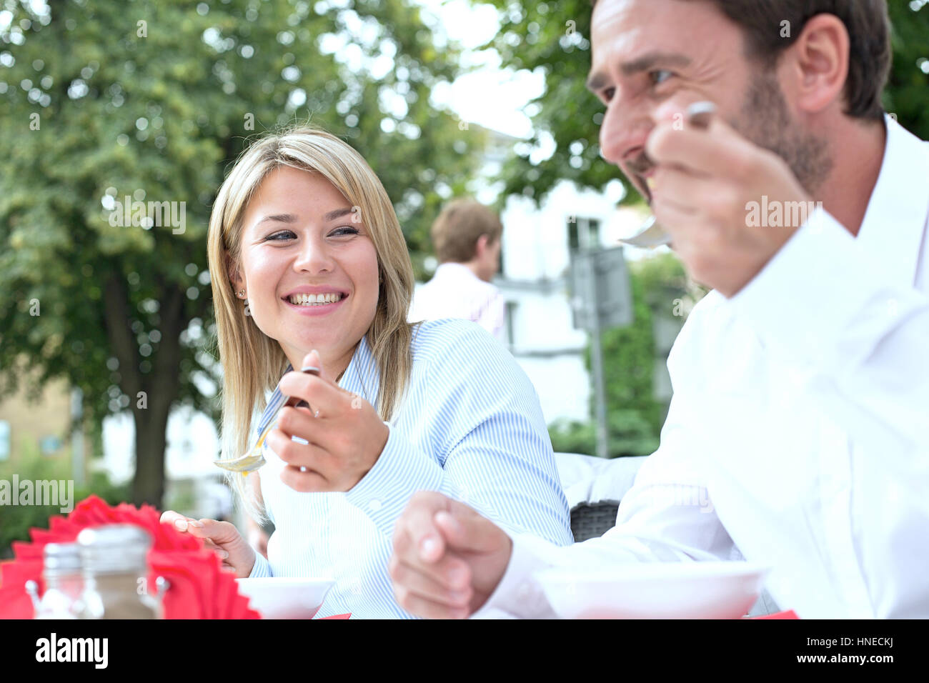 Happy businesswoman eating food with colleague at sidewalk cafe Stock ...