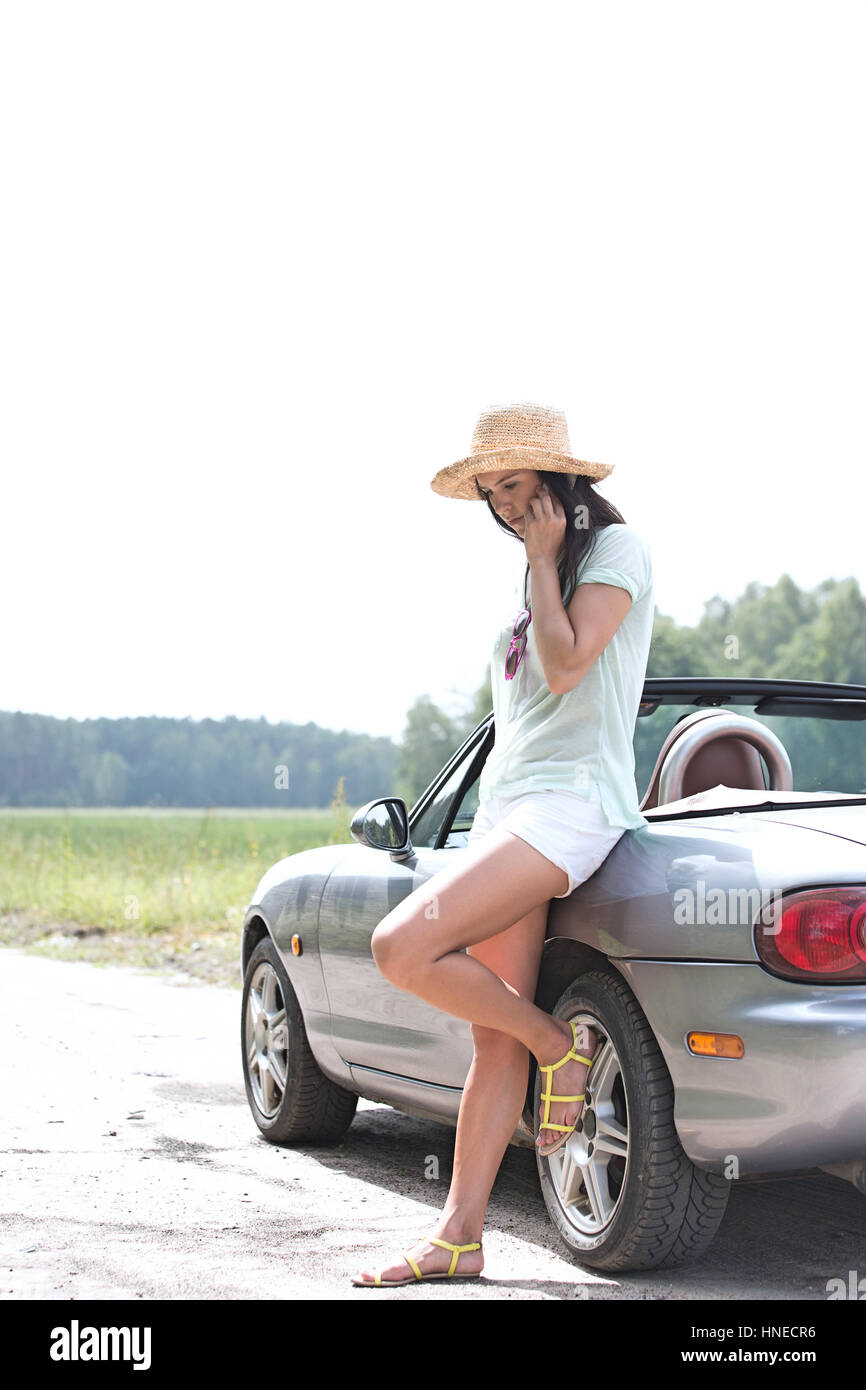 Full-length of woman using cell phone while leaning on convertible at ...