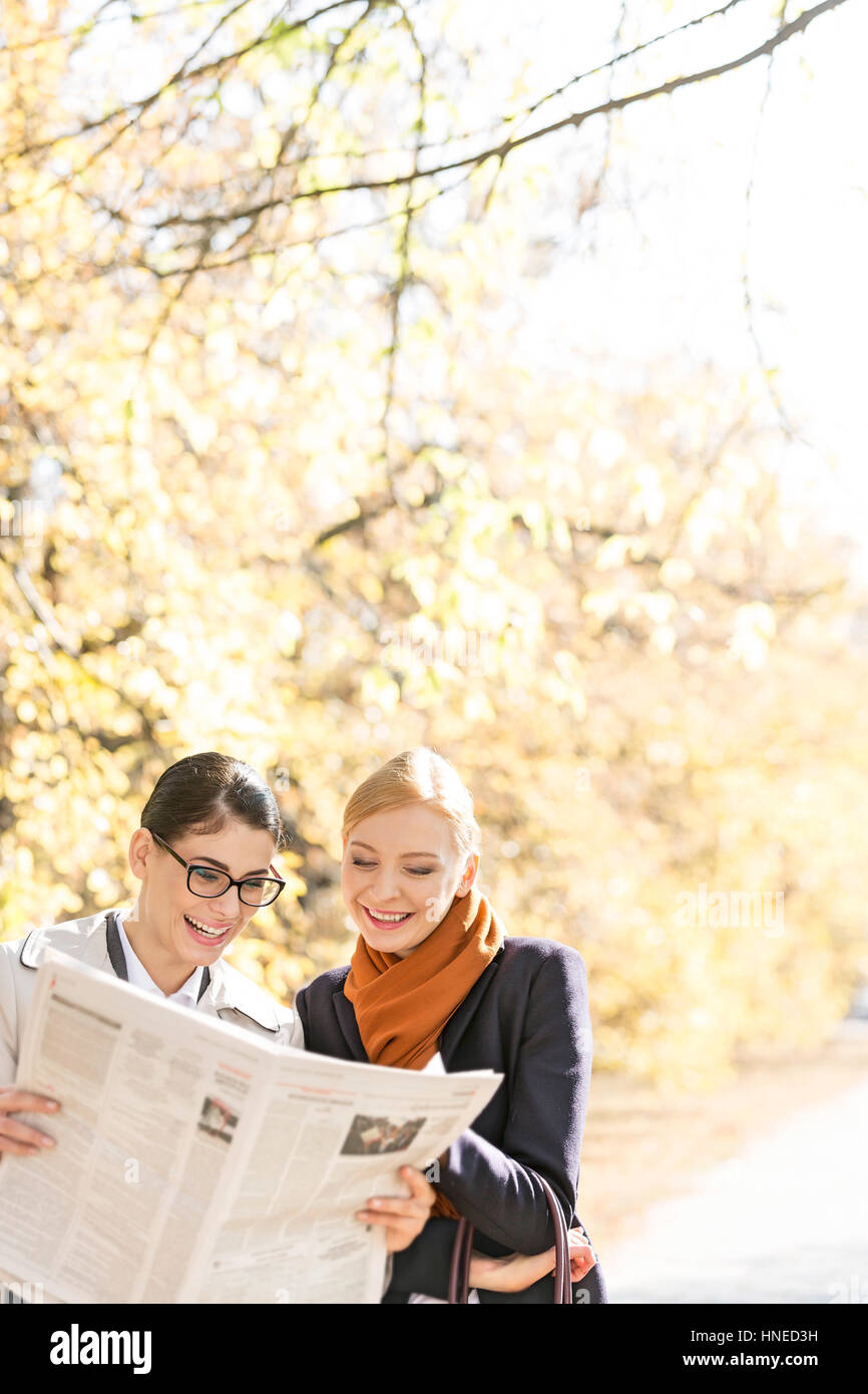 Happy businesswomen reading newspaper together at park Stock Photo - Alamy