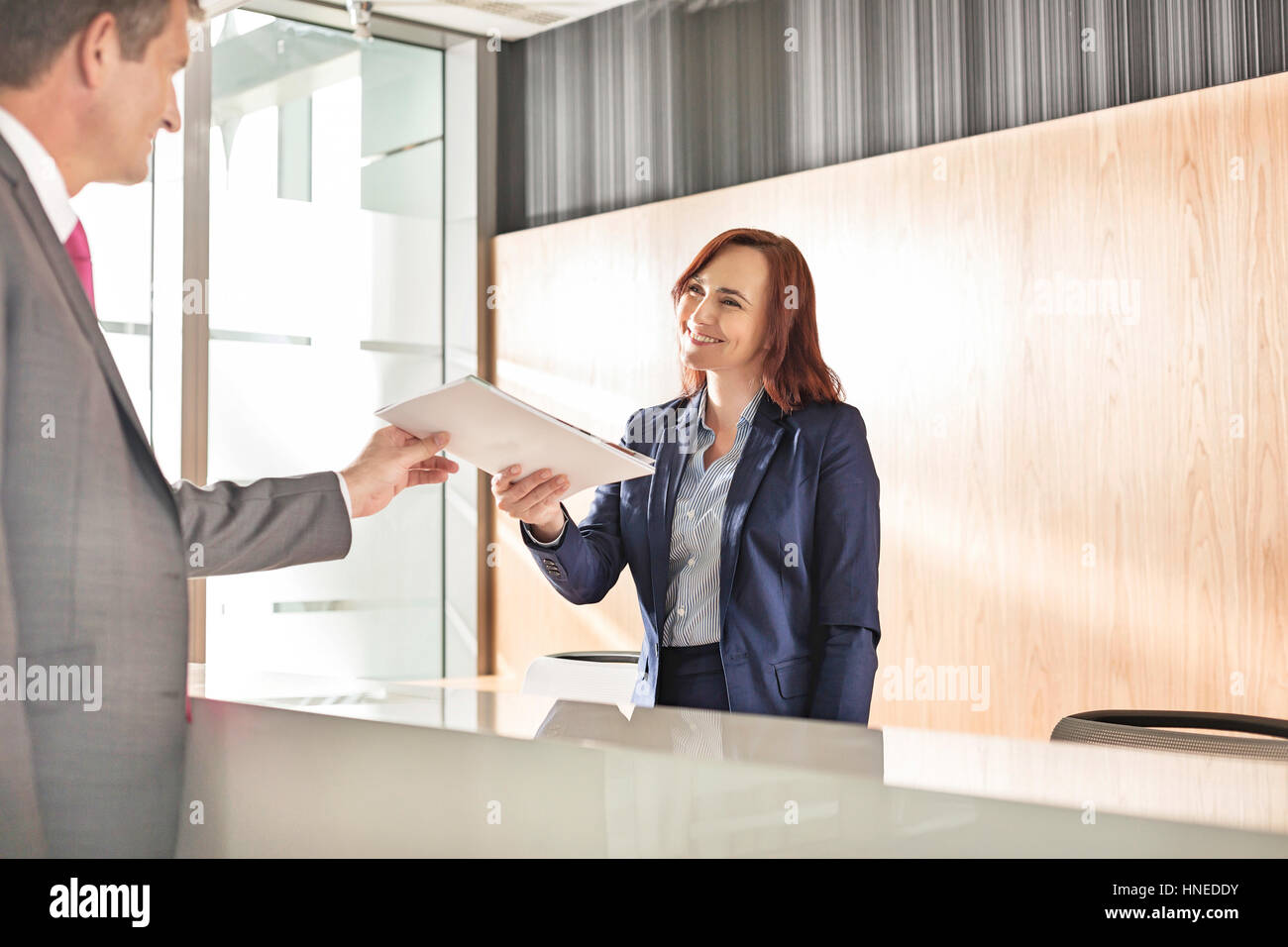 Businessman receiving document from receptionist in office Stock Photo ...