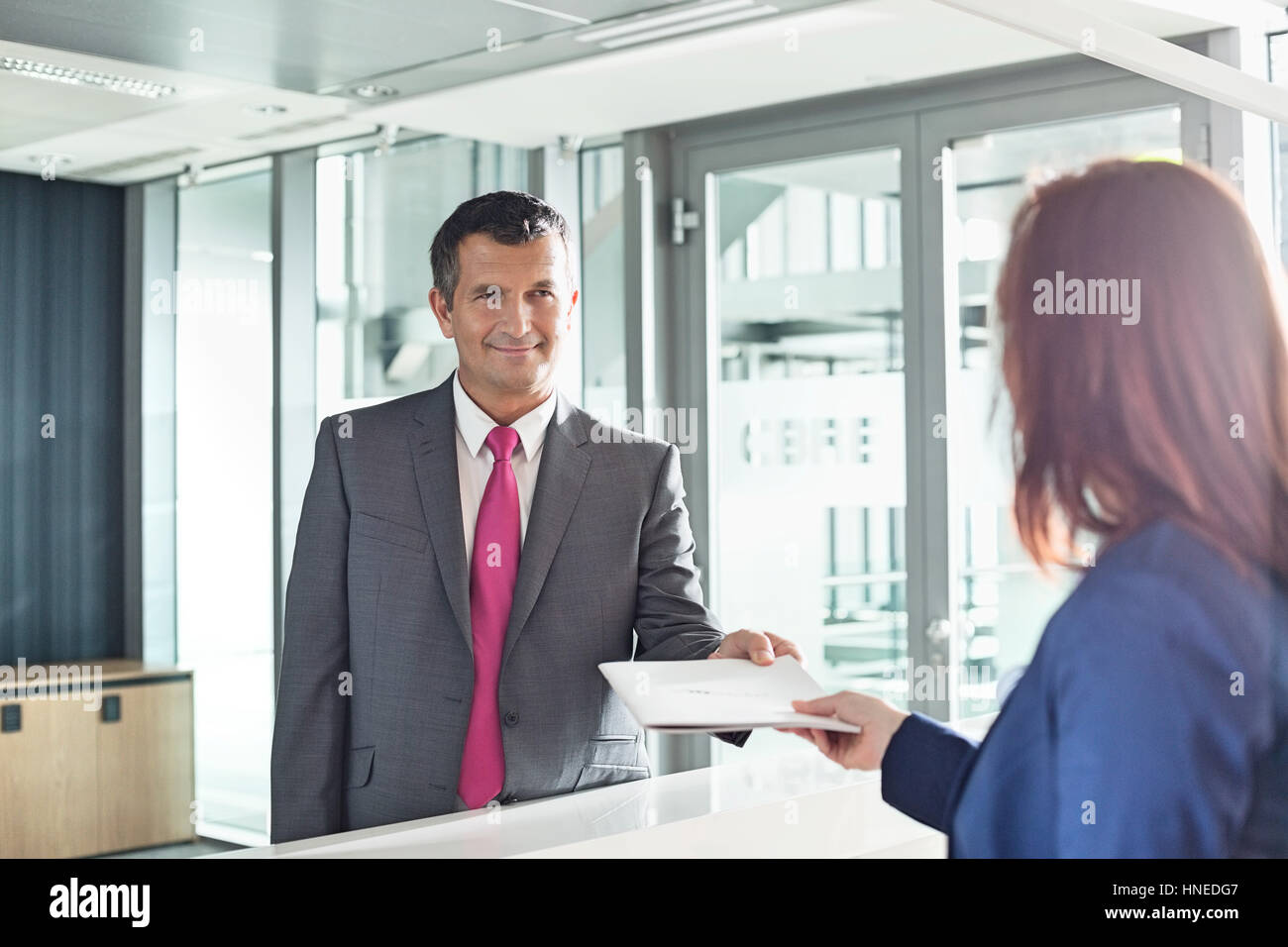 Businessman receiving document from receptionist in office Stock Photo ...